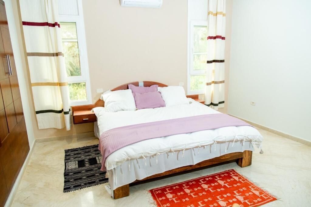 Quarto com cama, mesa de cabeceira e janela com cortinas.