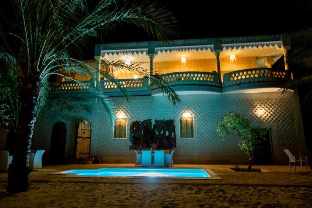 Um edifício com piscina, palmeiras e varanda iluminada.