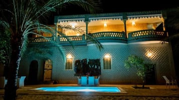 Um edifício com piscina, palmeiras e varanda iluminada.