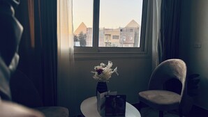 Um quarto com uma janela, um vaso com flores, uma cadeira e uma mesa com uma caixa.
