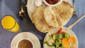 Mesa de café da manhã com pratos de comida, xícara de café e copos de suco de laranja.
