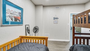 Quarto com duas camas, um quadro emoldurado de um porto, um ventilador e uma placa com a inscrição 'BEACH'.