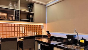 Uma cozinha moderna com bancada preta, pia e fogão embutido. Cadeiras e uma mesa de jantar também estão visíveis.