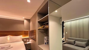 Quarto moderno com cama, mesa de cabeceira, aparador, guarda-roupa e um sofá cinzento.
