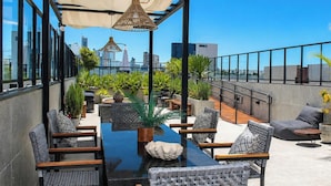 Terraço no telhado com mesa de jantar, cadeiras, plantas em vasos e vista para a cidade.