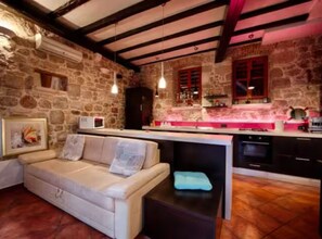 Uma sala de estar acolhedora com sofá, uma cozinha com parede de pedra e teto de madeira.