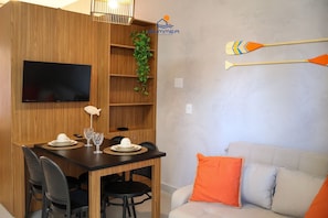Quarto moderno com mesa de jantar de madeira, cadeiras, televisão de tela plana, sofá com almofadas laranja e prancha de remo fixada na parede.
