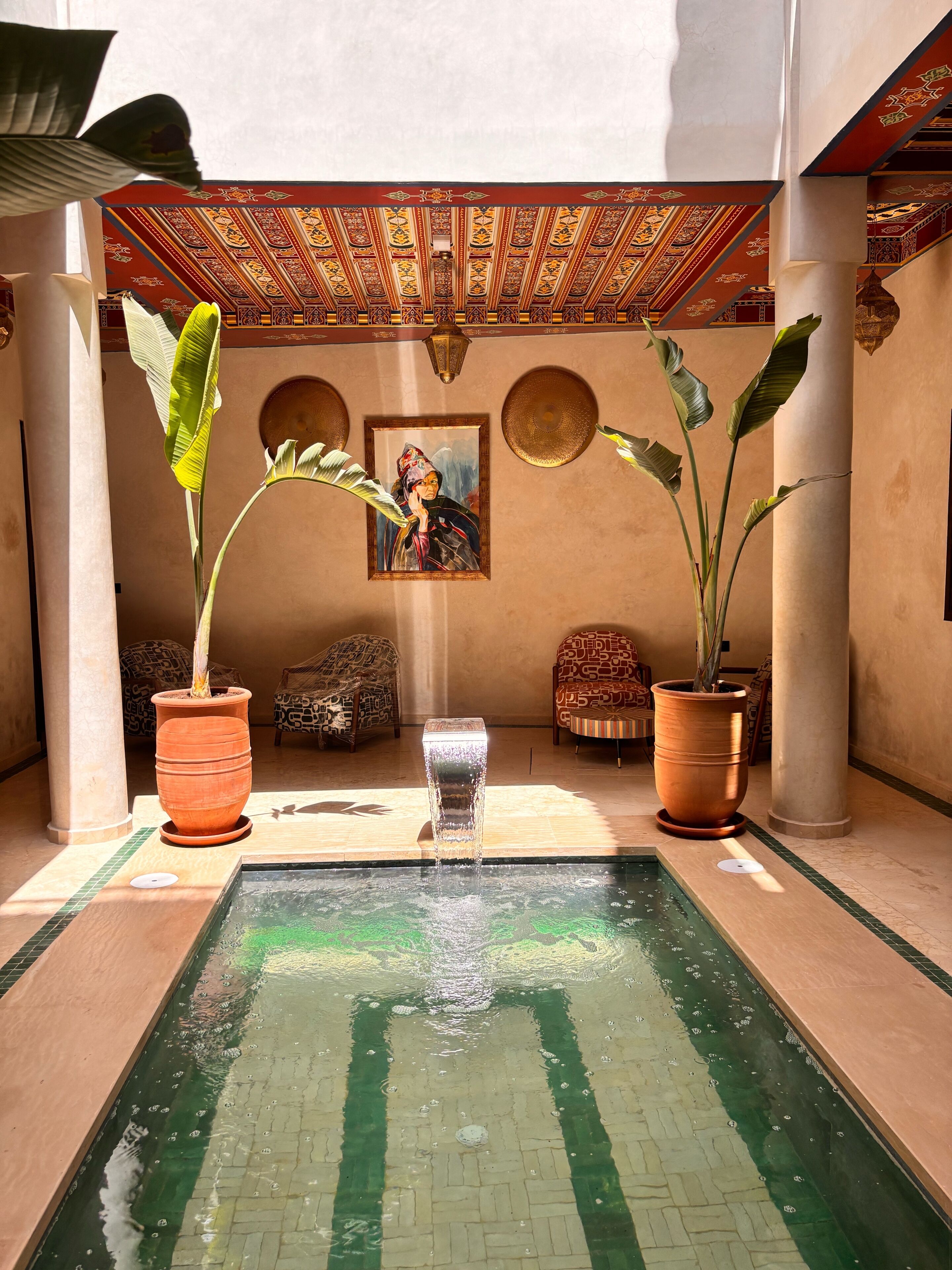 Uma área de piscina com uma fonte, plantas em vasos e paredes com padrão.