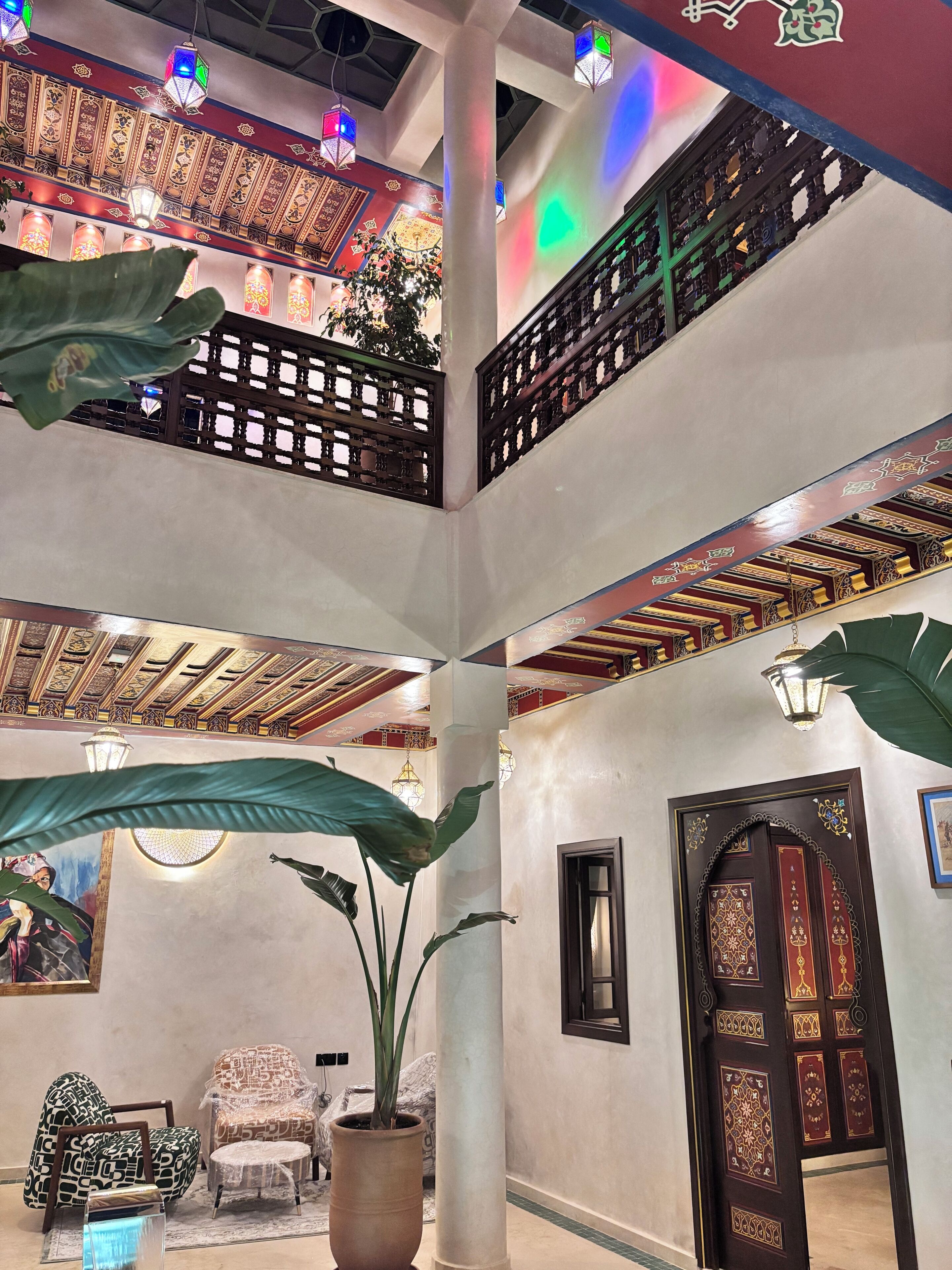 Interior com vários níveis, tetos ornamentados, uma grande planta em vaso e uma porta tradicional.