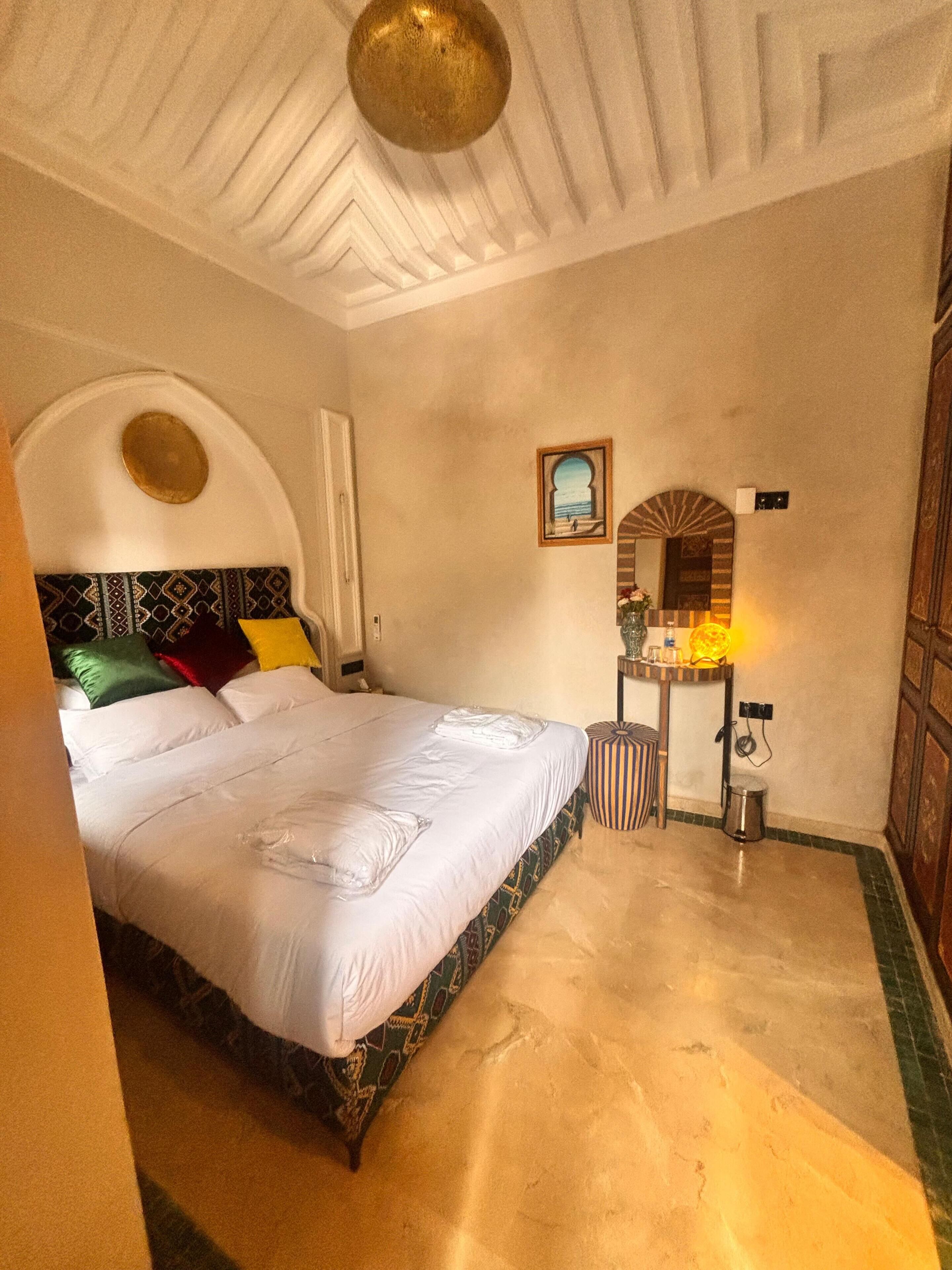 Um quarto com cama, mesa de cabeceira, luminária e espelho.