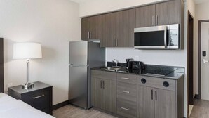 Uma cozinha de hotel compacta com geladeira, micro-ondas, fogão e uma pia pequena.