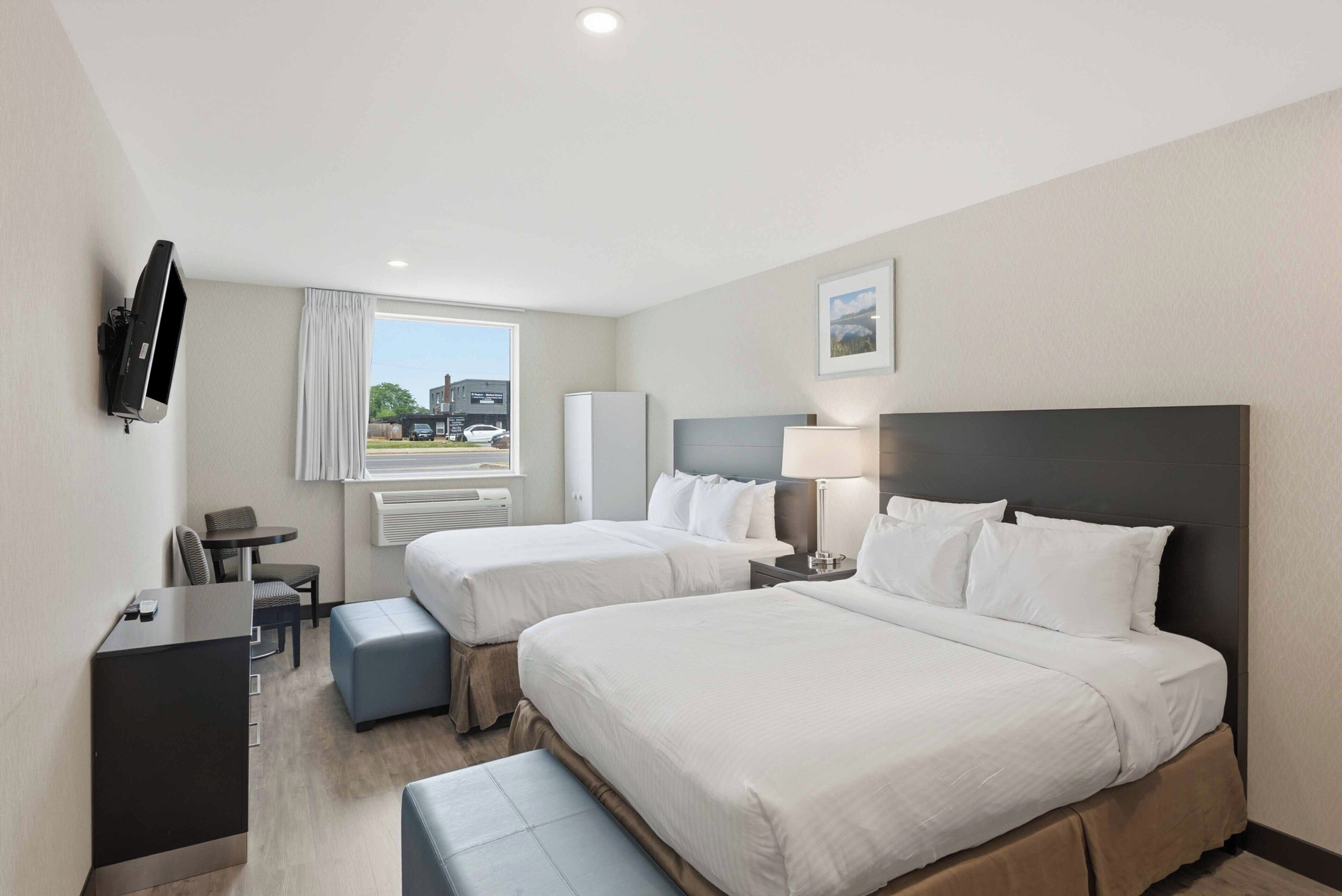 Quarto de hotel com duas camas, uma mesa, uma cadeira, uma televisão e uma janela.