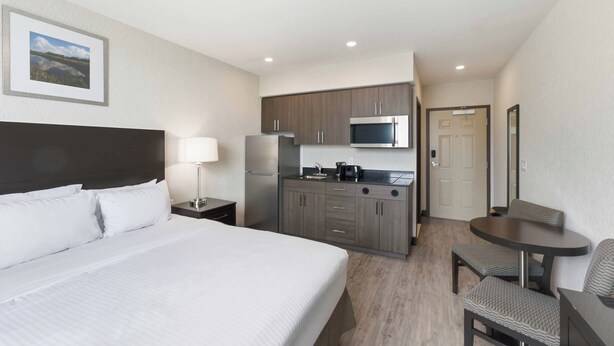 Quarto de hotel com cama, pequena cozinha, mesa de jantar com cadeiras e porta que dá para outro cômodo.
