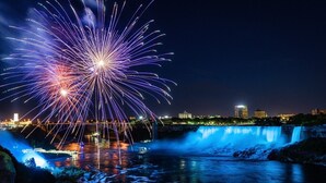 Uma cascata com uma ponte e fogos de artifício ao fundo.