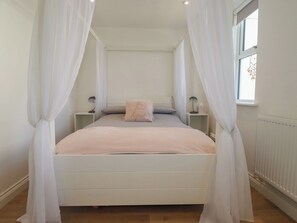 Quarto com cama, cortinas brancas, abajures e janela com vista.