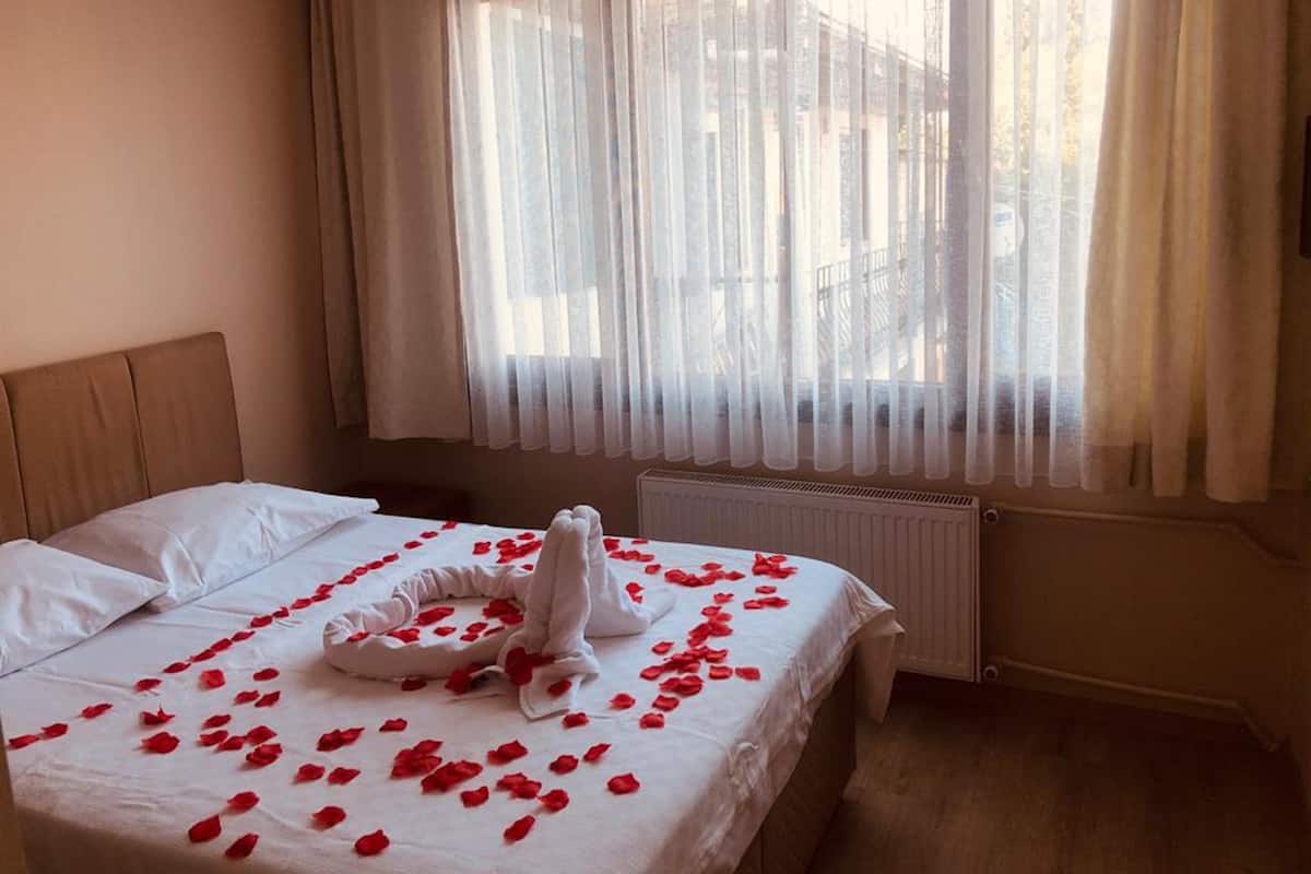 Quarto de hotel com uma cama, uma janela com cortinas leves e um radiador.