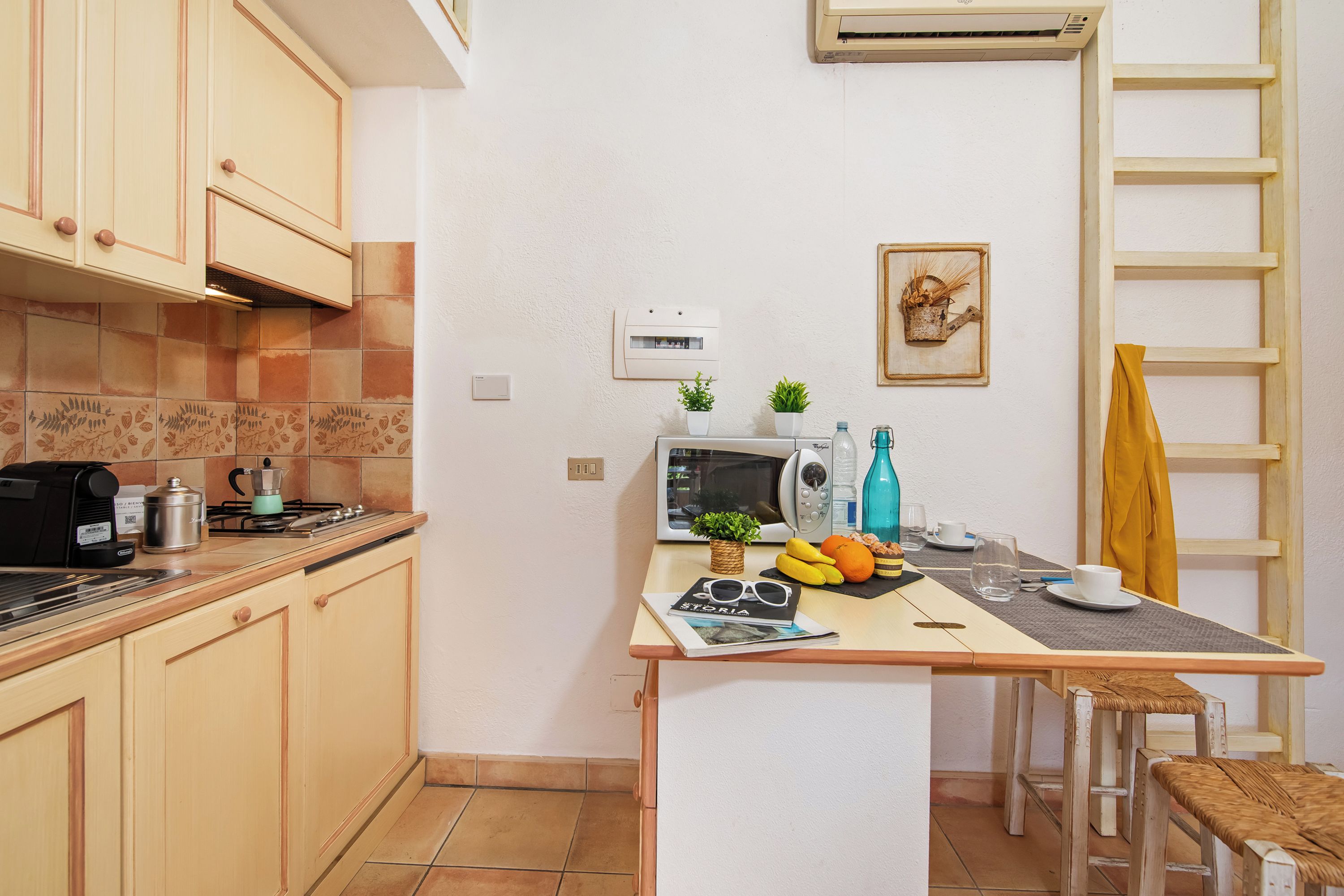 Uma cozinha compacta com micro-ondas, chaleira e um pequeno espaço de refeições com banquetas.