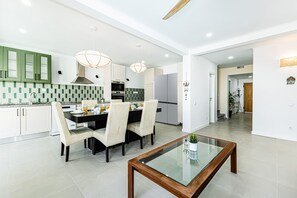 Cozinha moderna com armários brancos, área de refeições com mesa de vidro e corredor que dá acesso a outros cômodos.