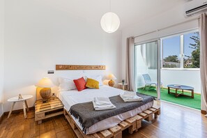 Quarto com cama, mesas de cabeceira, luminária, vista para o exterior e um aviso na parede.