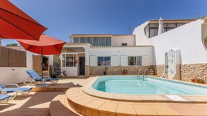Piscina com toldo de sol, cadeiras de praia e uma parede de pedra.