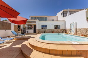 Piscina com toldo de sol, cadeiras de praia e uma parede de pedra.