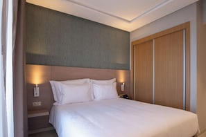Quarto de hotel com cama, abajures, guarda-roupa de madeira e parede estampada.