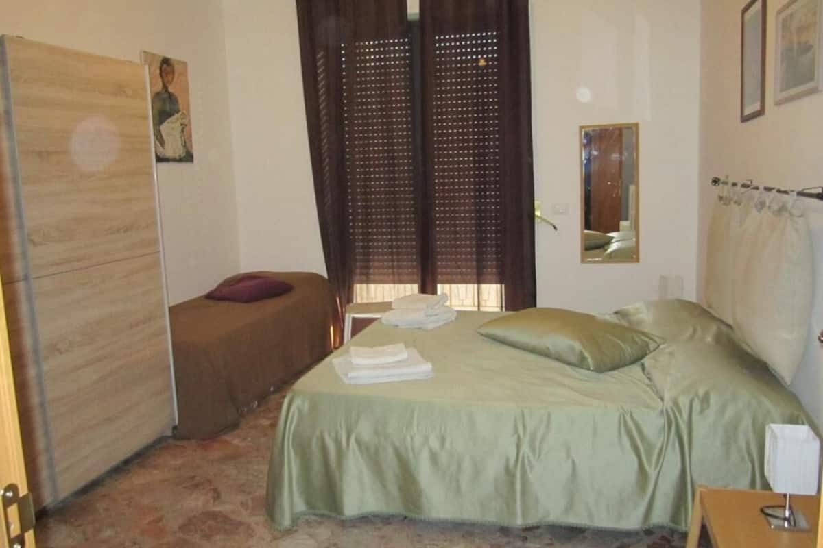 Quarto com cama, cadeira, guarda-roupa e janela com cortinas.