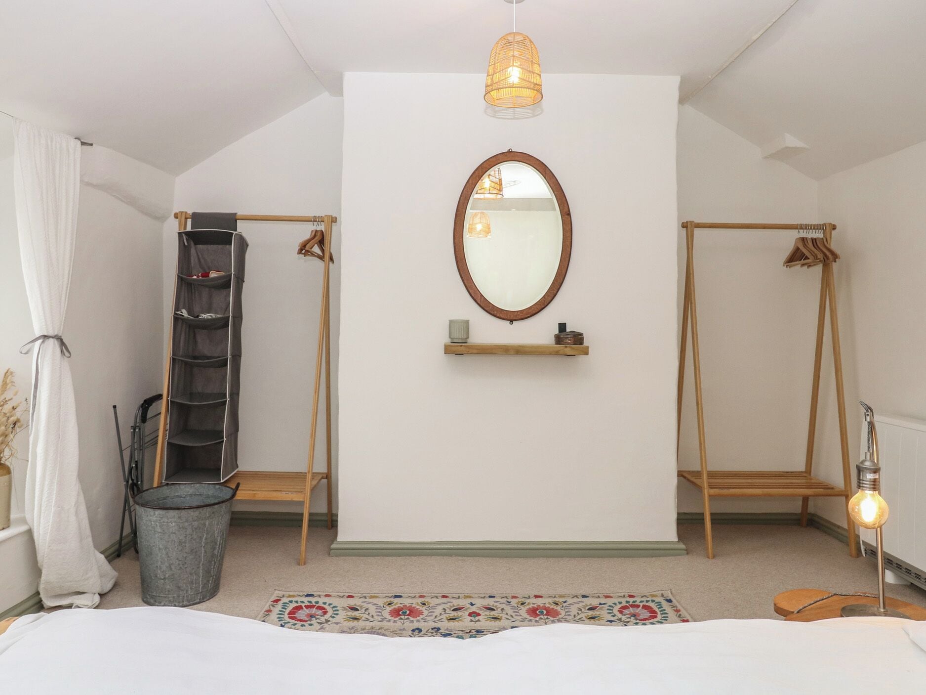 Quarto com cama, cadeira suspensa, prateleira com objetos, espelho, luminária e radiador.