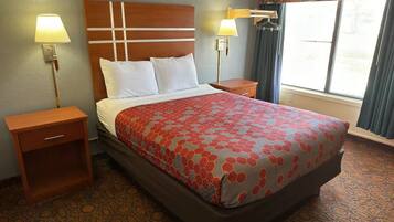 Quarto de hotel com uma cama grande, duas mesas de cabeceira, duas luminárias de parede, uma janela com cortinas e um tapete estampado.