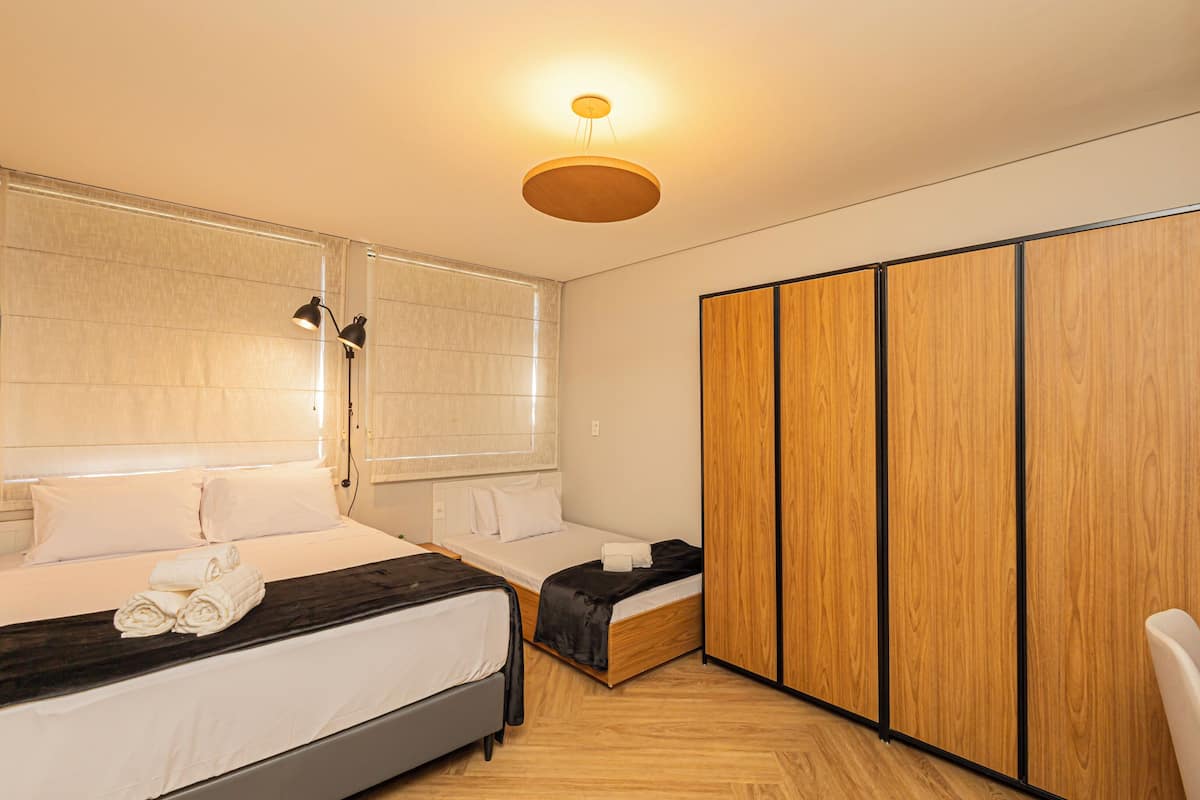 Quarto de hotel com cama, mesa de cabeceira, guarda-roupa e luminária no teto.