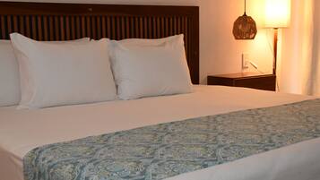 Cama bem arrumada com colcha estampada, cabeceira de madeira e abajur.