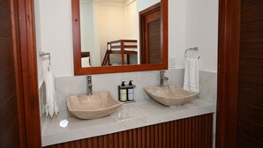 Um banheiro com duas pias bege, um espelho com moldura de madeira e um porta-toalhas.
