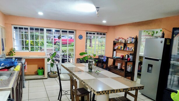 Cozinha com piso de azulejos, ilha central com banquetas, geladeira e janela com vista para vegetação.