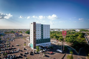 Hotel com vários andares, estacionamento em frente, rodeado por vegetação e céu claro.