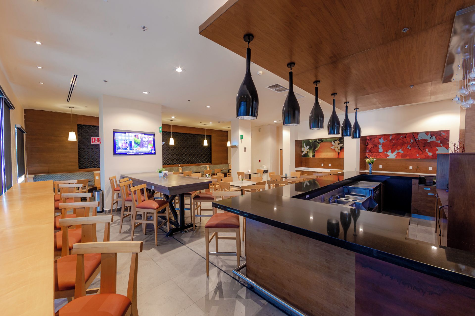 Restaurante moderno com balcão central, várias mesas de jantar e uma tela de televisão exibindo conteúdo.