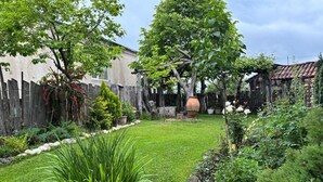 Um jardim com diversas plantas, um cercado de madeira e um edifício rústico.