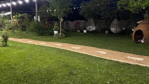 Área externa bem iluminada com um caminho, luzes de festa e cadeiras suspensas.