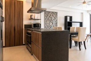 Cozinha moderna com ilha integrada, armários de madeira, eletrodomésticos de aço inoxidável e área de jantar com mesa e cadeiras.
