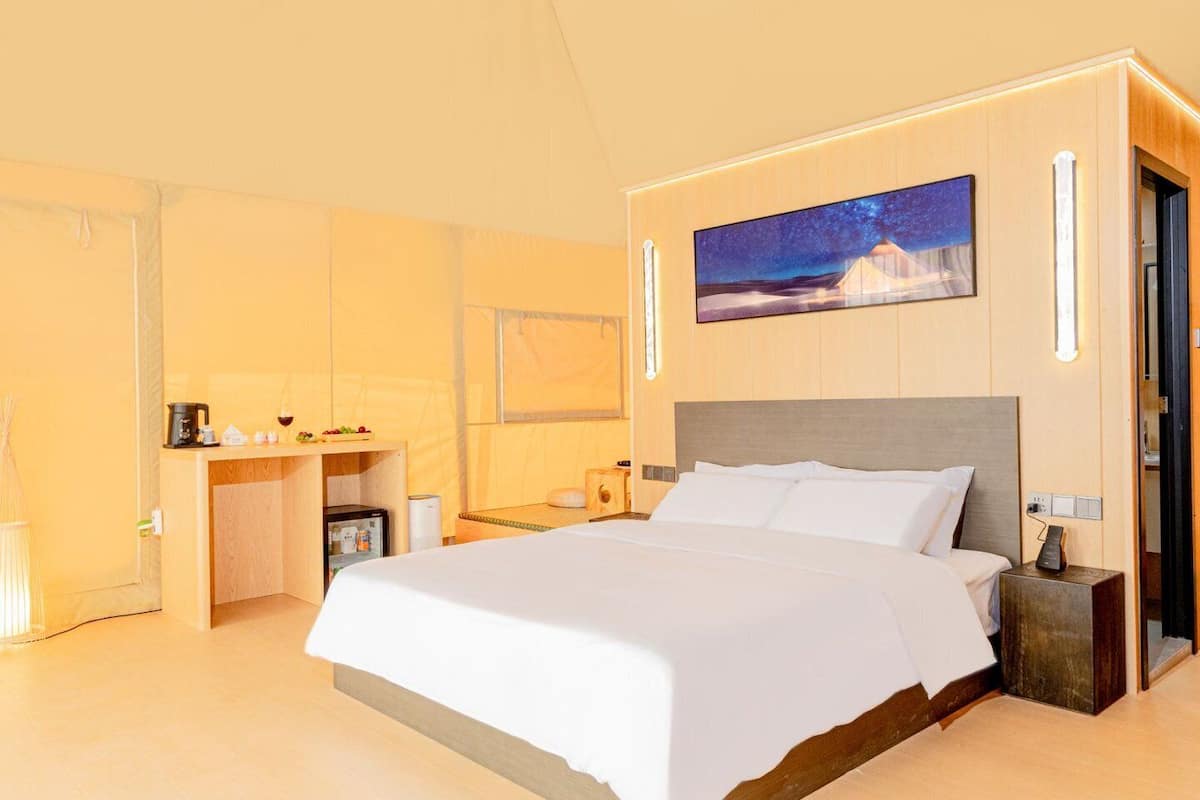 Quarto de hotel com cama, mesa de cabeceira, criadeira e um quadro de uma cena noturna.