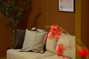 Um sofá bege com almofadas estampadas, um vaso de planta e um quadro na parede.