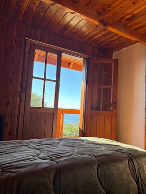 Um quarto de madeira com uma janela grande, uma cama e uma porta.