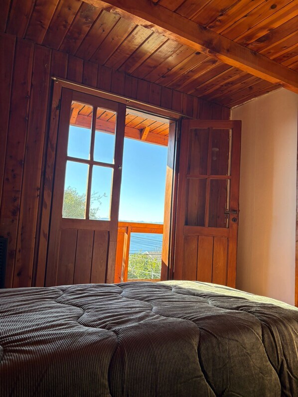 Um quarto de madeira com uma janela grande, uma cama e uma porta.