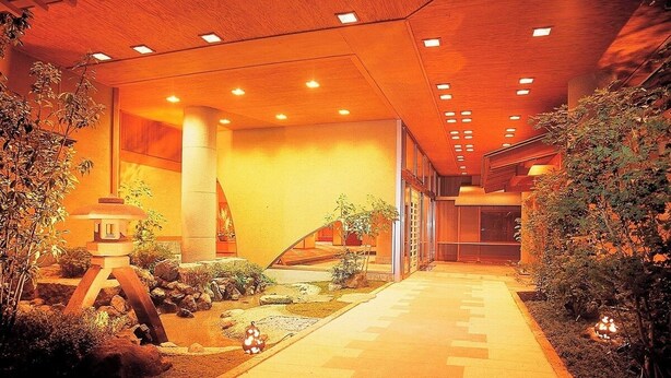 Uma trilha leva a um edifício de design moderno, com teto de madeira e interior bem iluminado.