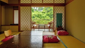 Um quarto japonês tradicional com tatames, uma mesa baixa e vista para um jardim exuberante através de uma porta deslizante.