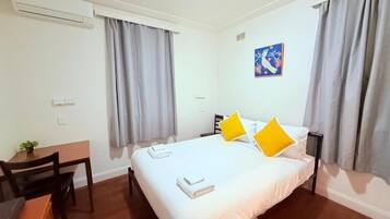 Quarto de hotel com uma cama, uma escrivaninha e uma cadeira.