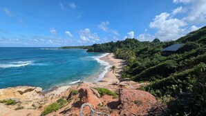 Paisagem costeira com praia, terreno rochoso e vegetação densa.