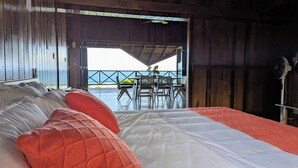 Quarto com cama, mesa e cadeiras, e vista para o oceano.
