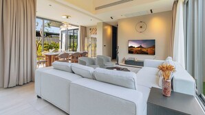 Uma sala de estar moderna com um sofá, uma mesa de centro e uma televisão. Há uma área de jantar com uma mesa e cadeiras.