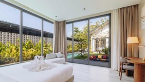 Quarto de hotel com uma cama grande, área de jantar e vista para uma piscina e área externa com mesas.