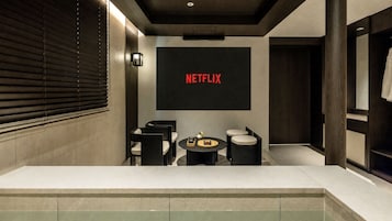 Uma casa de banho moderna com um espelho grande, uma pia e um ecrã fixado na parede a exibir 'NETFLIX'.